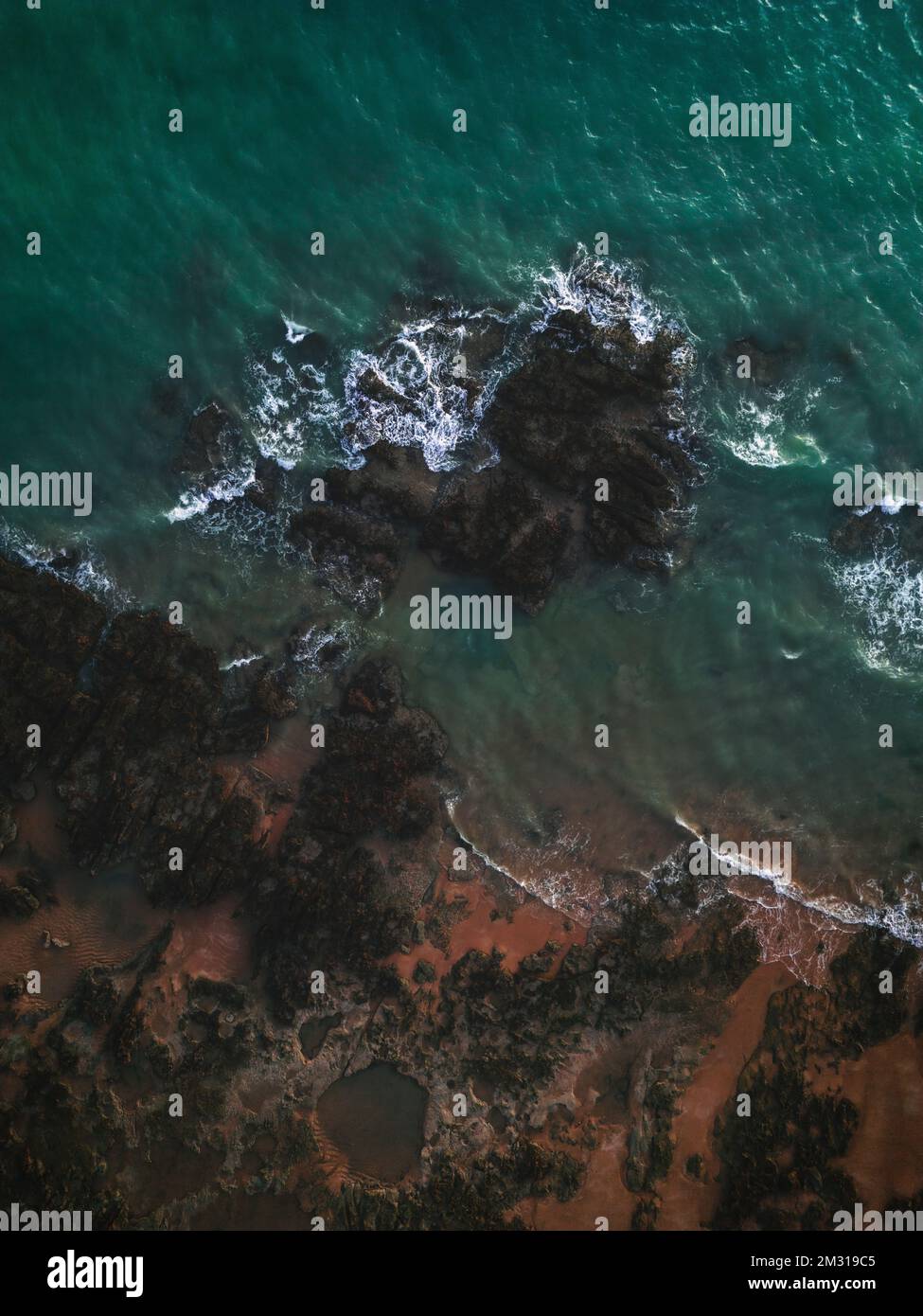 An aerial view of soft ocean waves splashing over the rocks on the ...