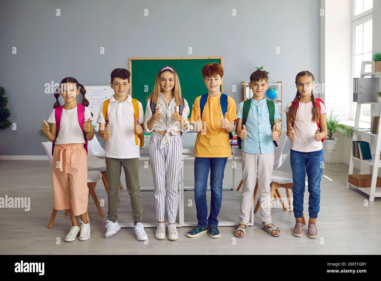 Happy group of schoolchildren ready for school showing thumbs up ...