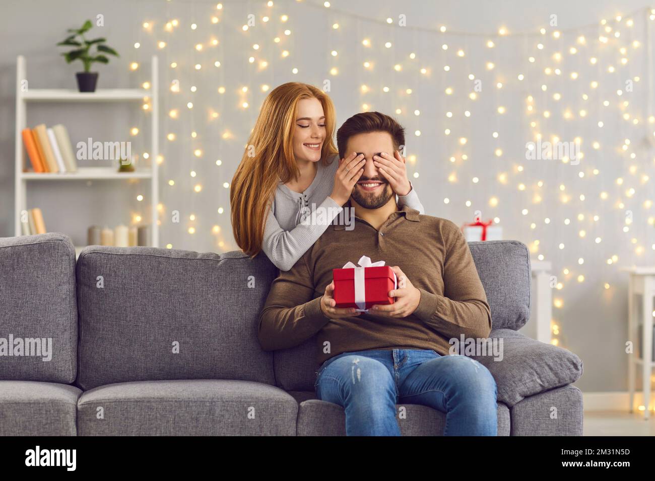Cute red-haired woman closes her boyfriend's eyes with her hands and ...