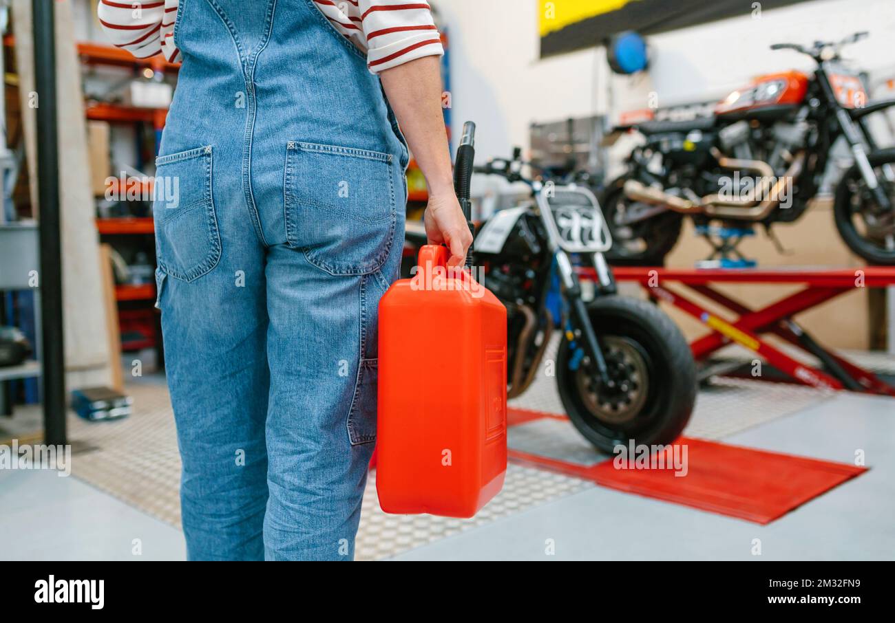Back view of mechanic woman holding jerry can in front of motorcycles ...