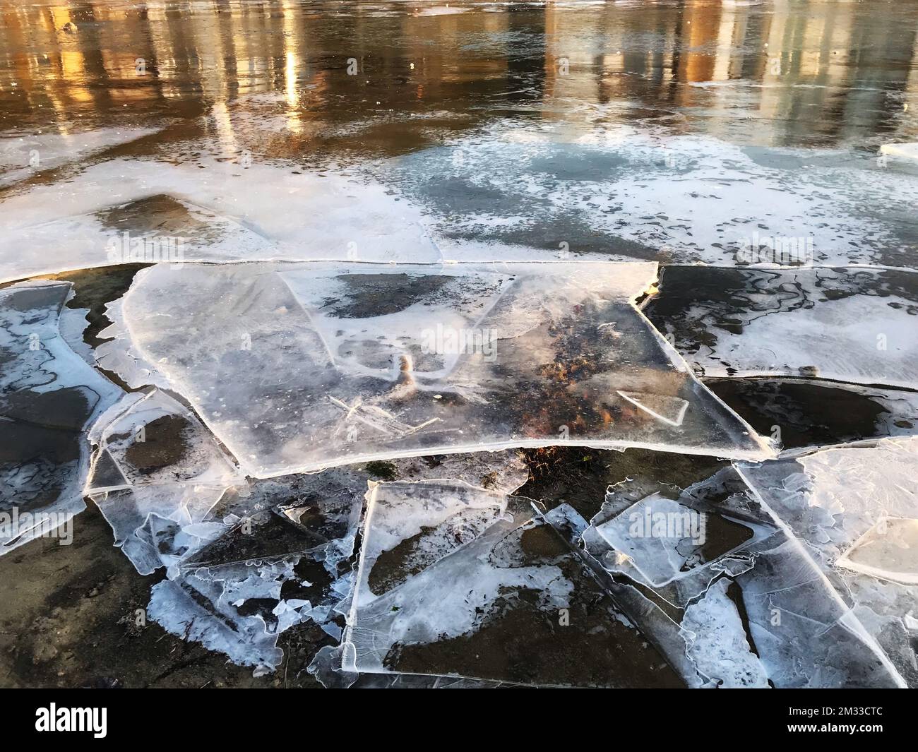 Sheets of ice lie broken on a boating lake duck pond winter seasonal ...