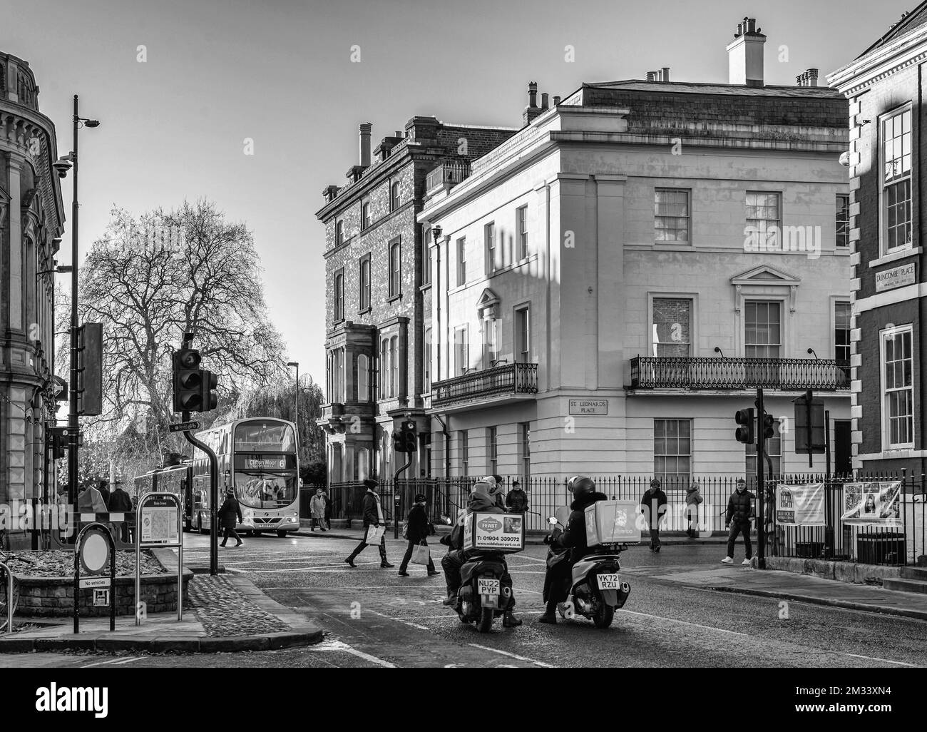 Two delivery riders stop at a road junction with historic buildings ...