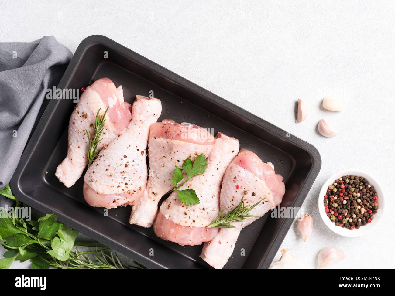 Raw chicken drumsticks in black baking form with seasonings over white ...