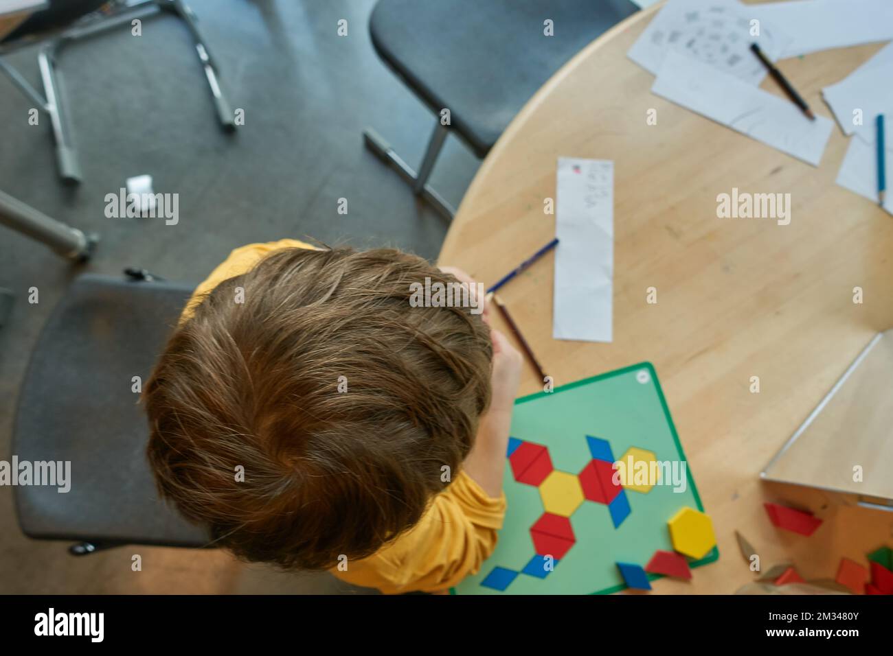 overhead view of a young boy working on arranging shapes into an object ...