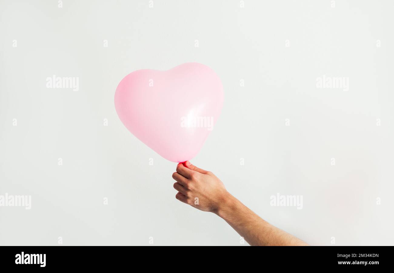 Pink inflatable heart-shaped balloon in hand. White background Stock ...