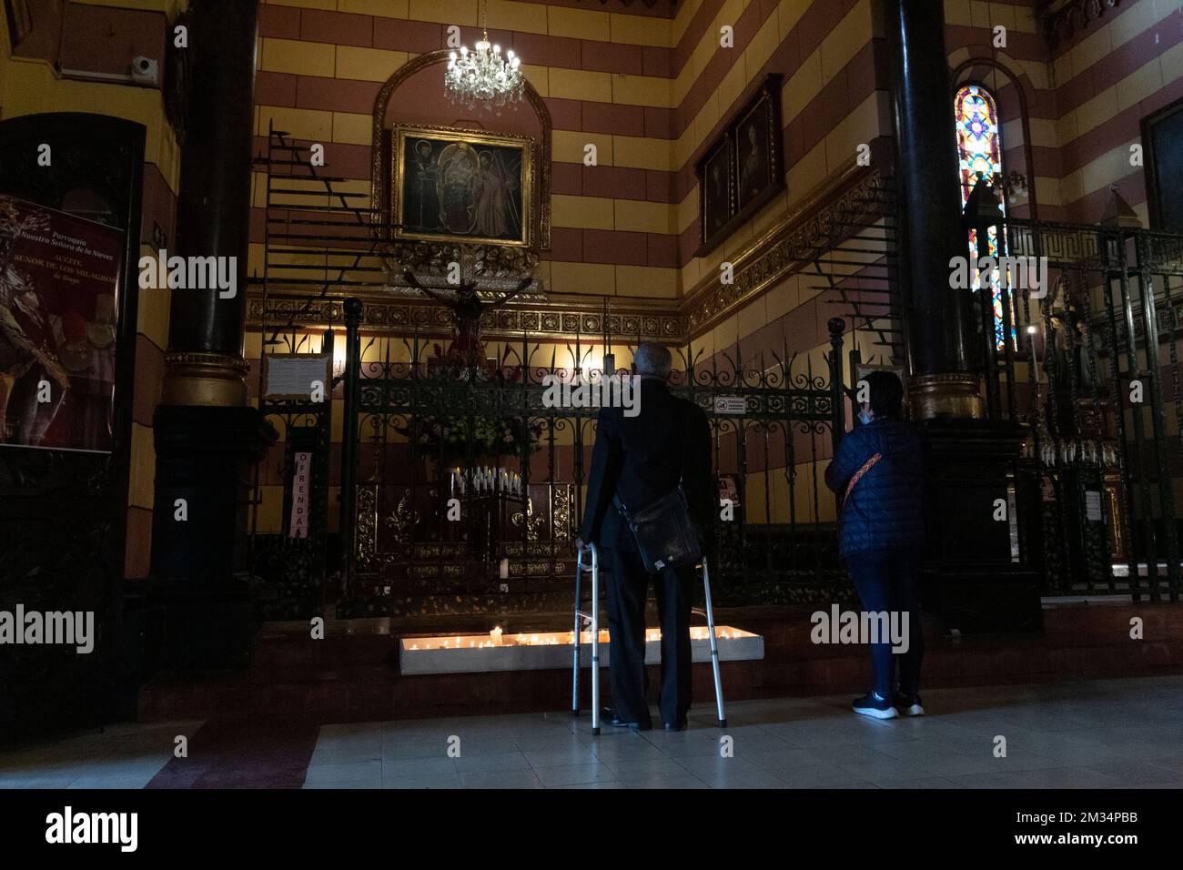 And old man and a lady in front of a small chapel with candles praying ...