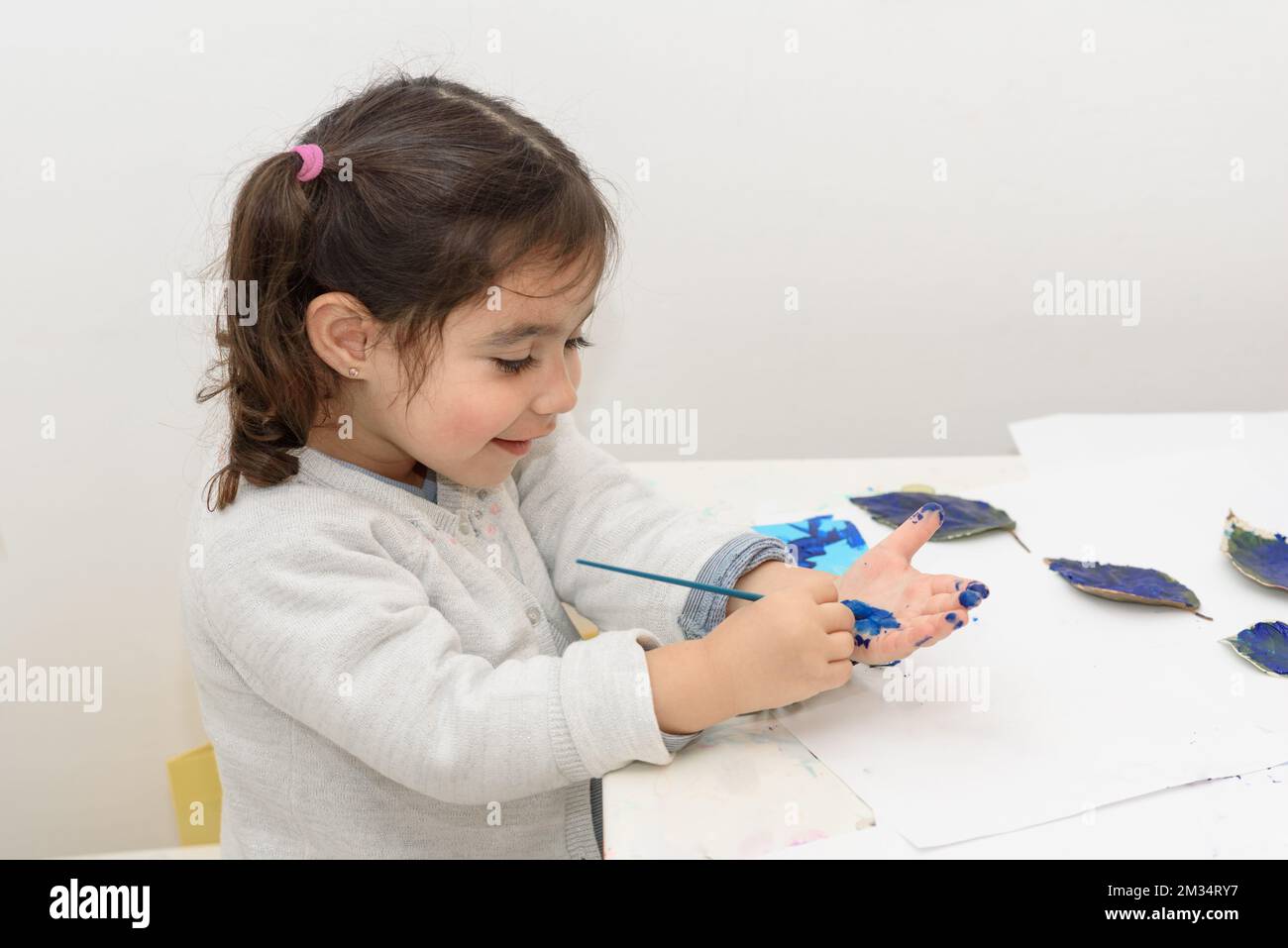 Little girl painting leaves blue color, crafts and art therapy. Child ...