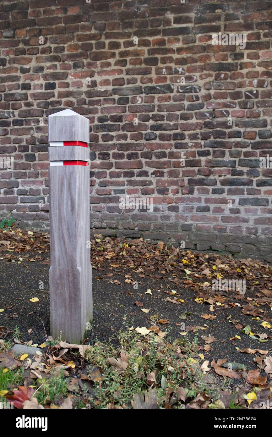 a wooden boundary post on a pedestrian area. with red and white labels ...