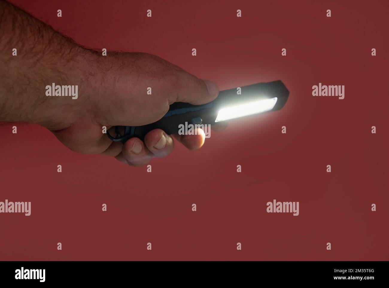 Pocket led flashlight in hand. illuminates red background. Copy space ...