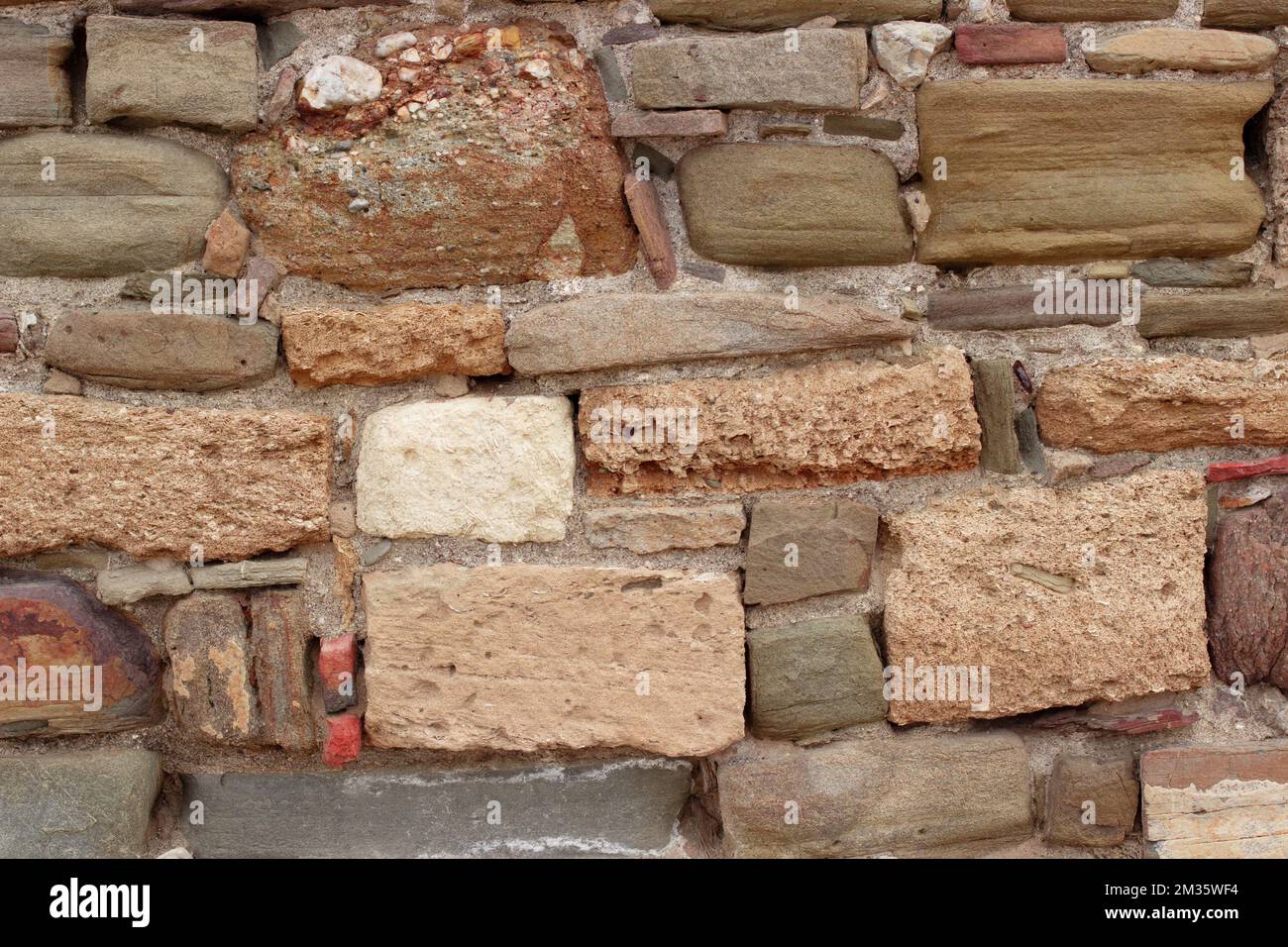 Old stone wall made of various square natural stones in beige, ocher ...