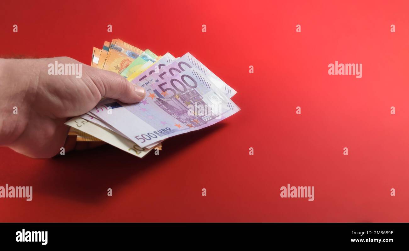 Cash money in a man's hand on a red table background. Hand holding euro ...