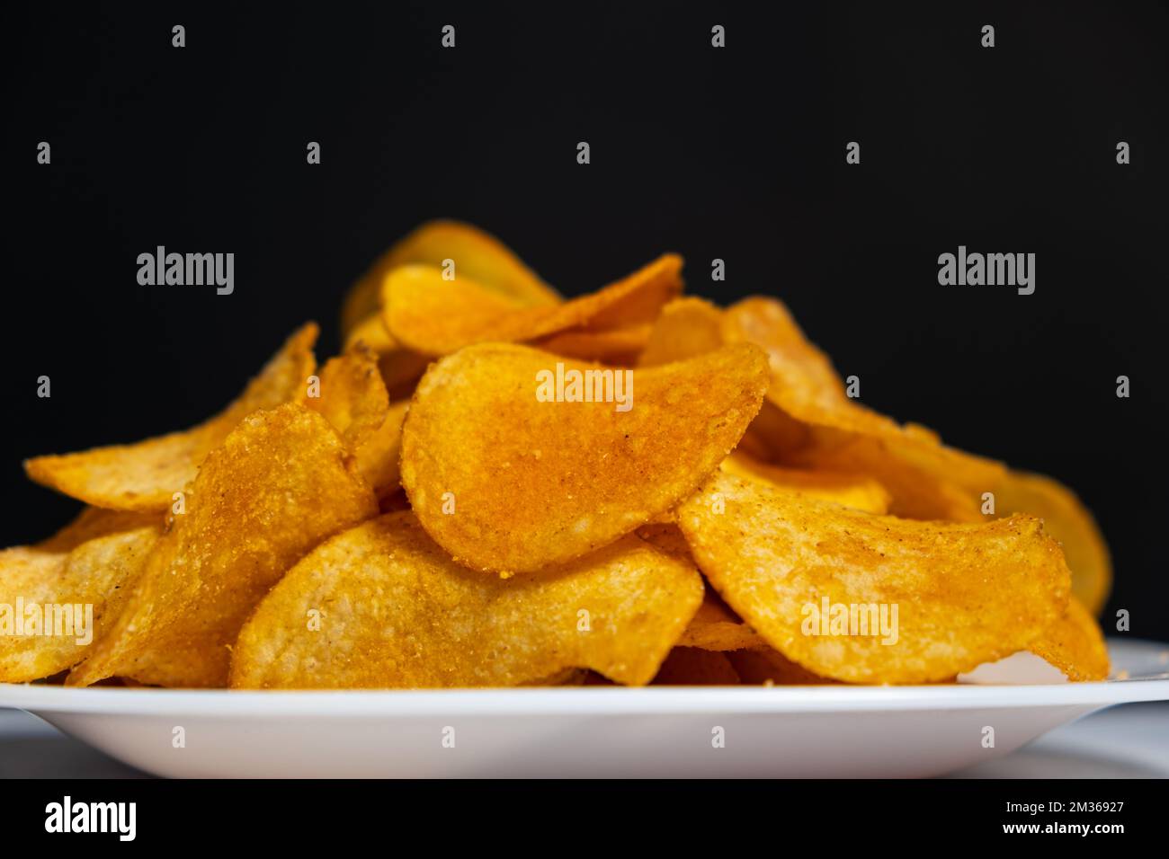 Thin crispy potato chips on a plate on a black background Stock Photo - Alamy