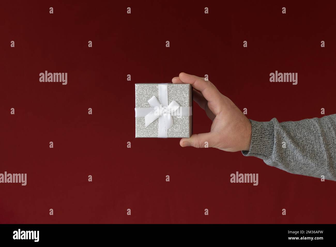 Gift time. A man's hand holds a Christmas gift box on a red-burgundy ...