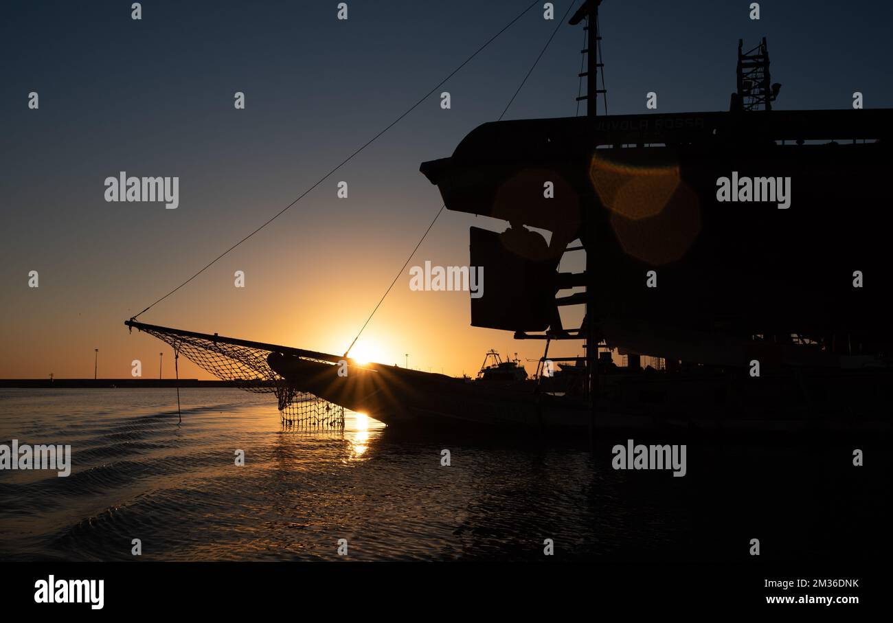 An old fishing boat lies at the harbor in front of a large metal ship ...