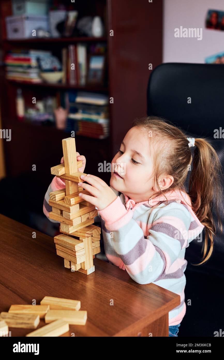Little girl preschooler playing with wooden blocks toy building a tower ...