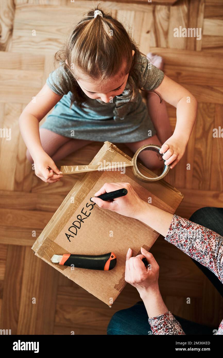 Woman writing an address on a cardboard box parcel in room at home ...