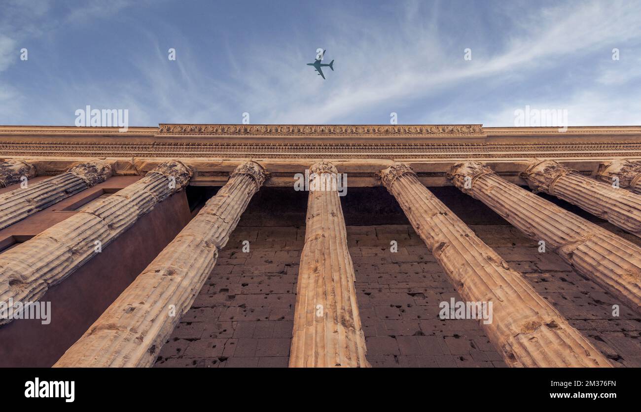 A low angle shot of the ancient columns and an aeroplane flying in the ...