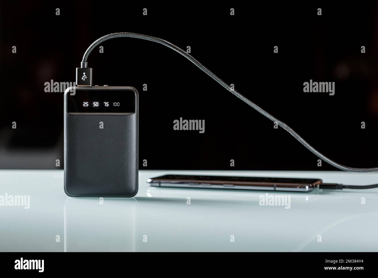Black powerbank with a black cord charging smartphone. Extra power ...