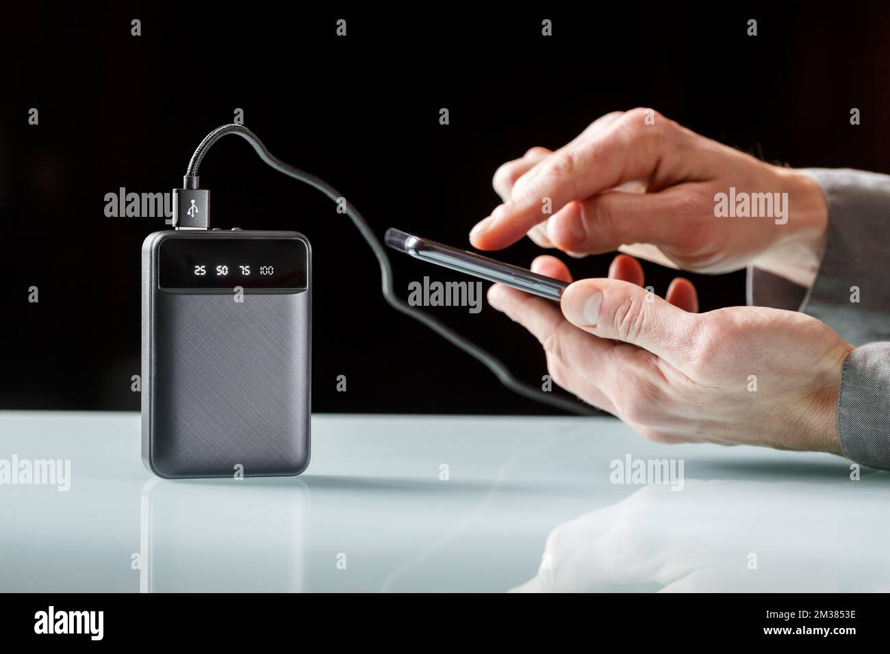Black powerbank with a black cord charging smartphone in a male hands ...