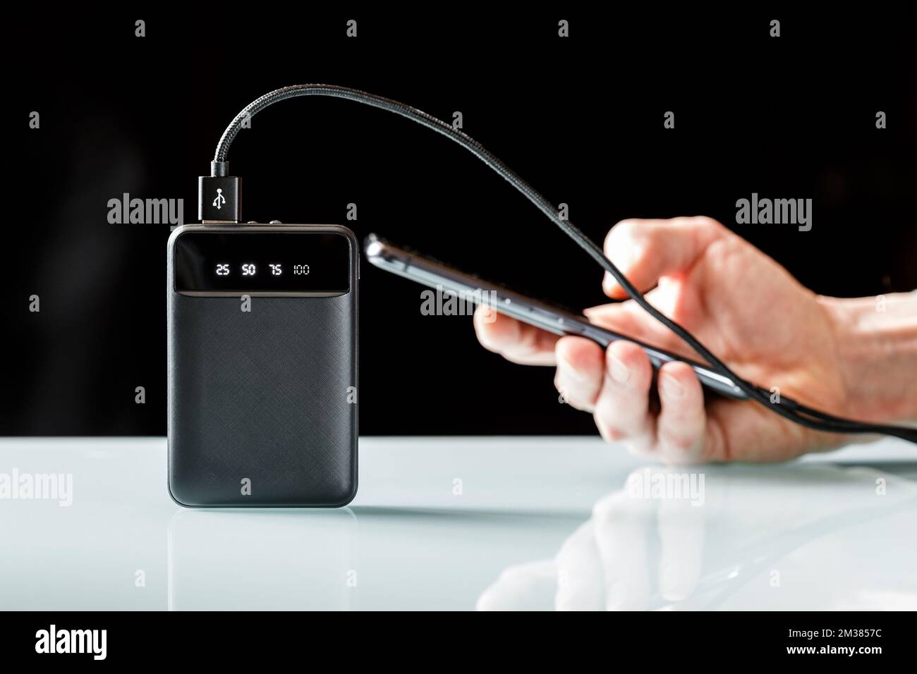 Black powerbank with a black cord charging smartphone in a male hands ...