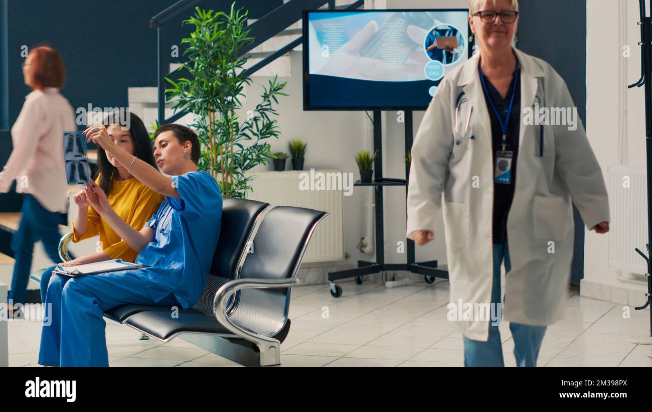 Medical assistant explaining radiography scan to asian patient, looking at bones x ray results ...