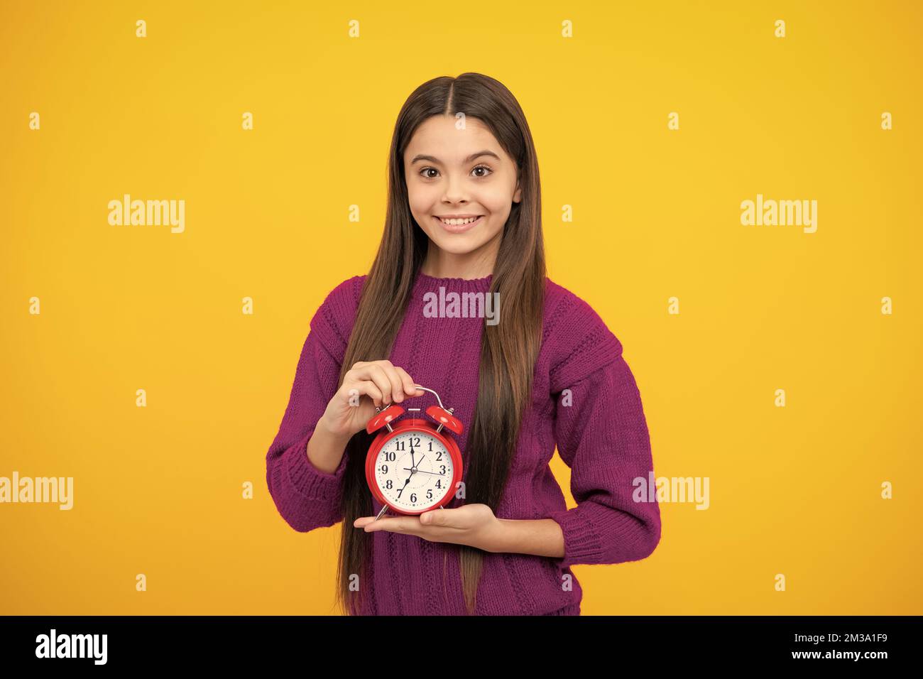 Teenager child hold clock isolated on yellow studio background ...