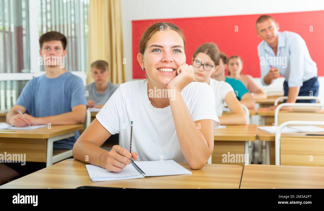 Smiling girl high school student listening to teacher during lesson ...