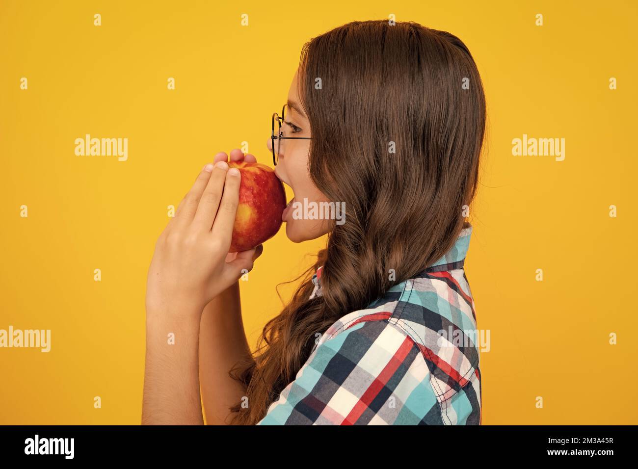 Child girl eating an apple over isolated yellow studio background ...