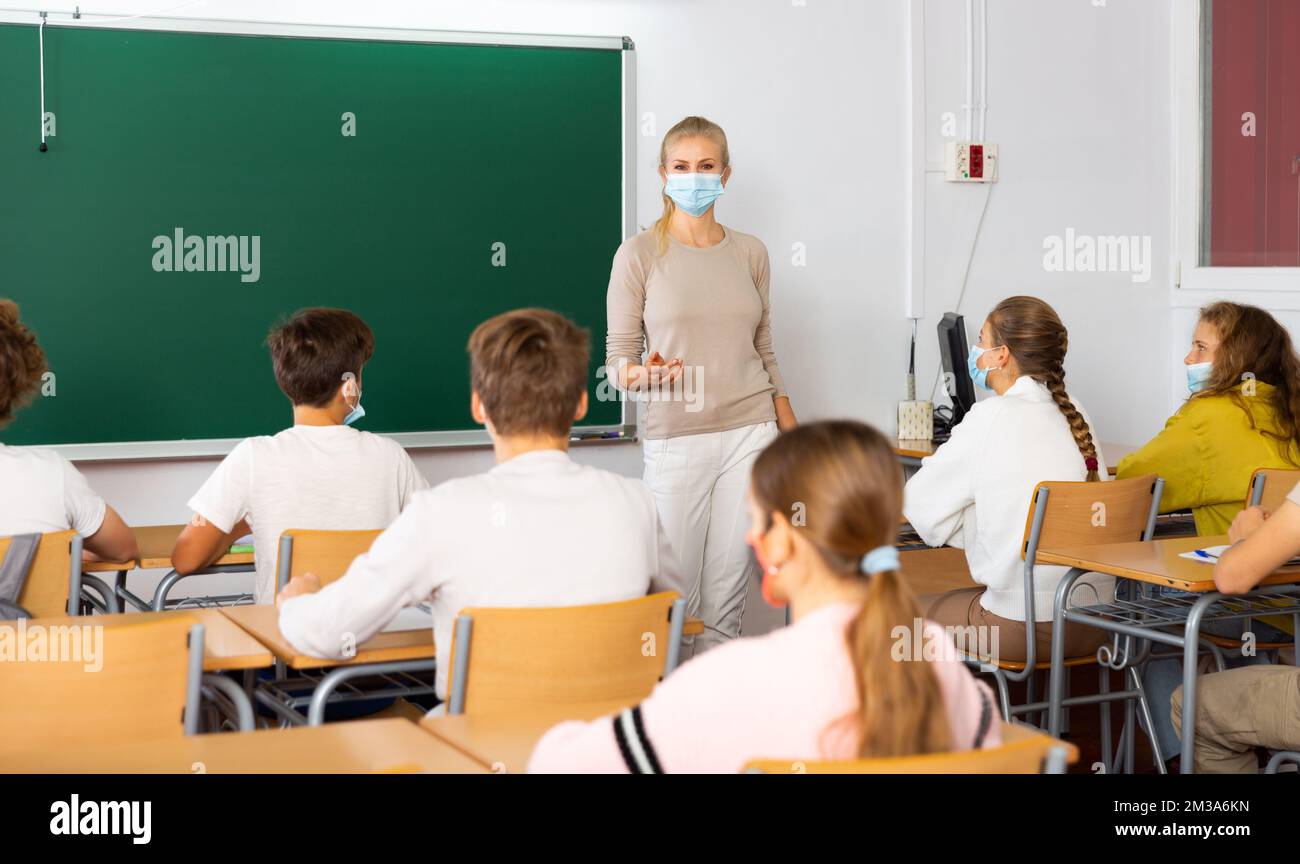 Female speaker in protective mask giving lesson for teenage students ...
