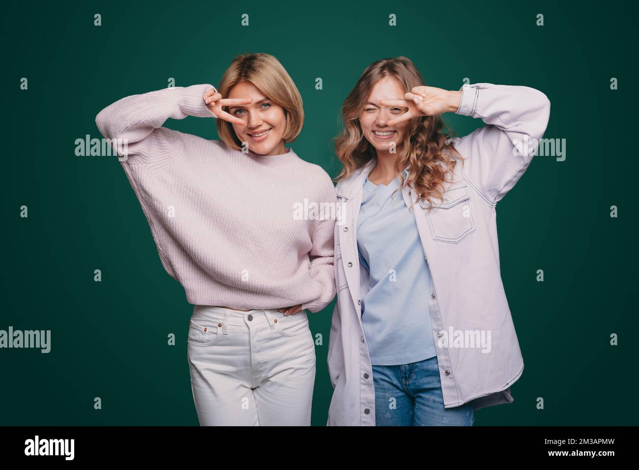 Photo of pretty two women showing v-sign symbols looking at camera ...