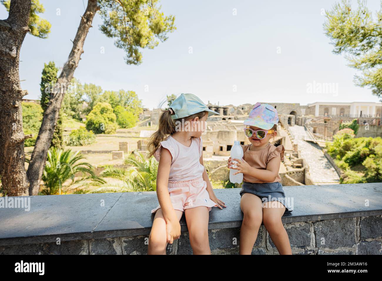 Two baby girl sisters sitting against panoramic view of the ancient ...