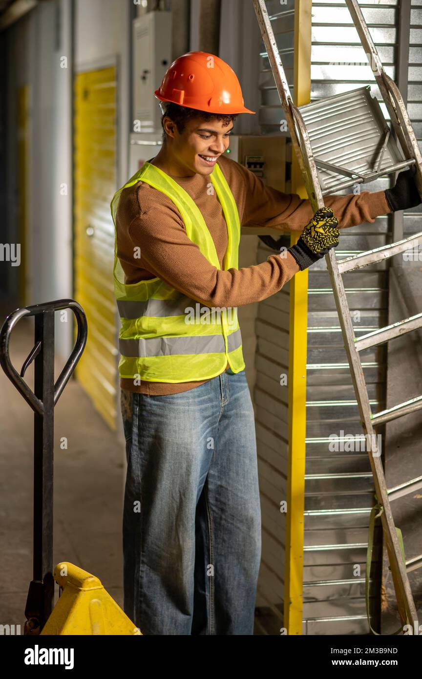 Smiling warehouse worker with the ladder Stock Photo - Alamy