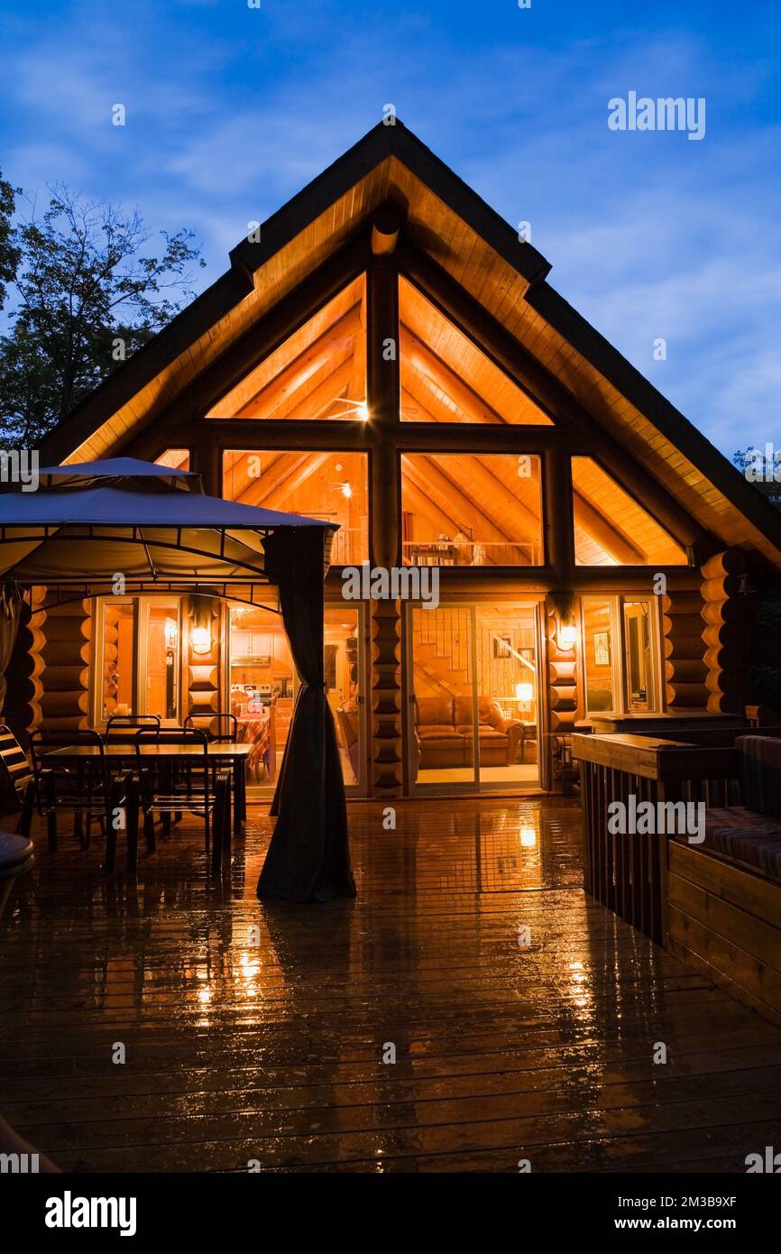 A-frame style log cabin with watered down wooden deck at dusk in summer ...