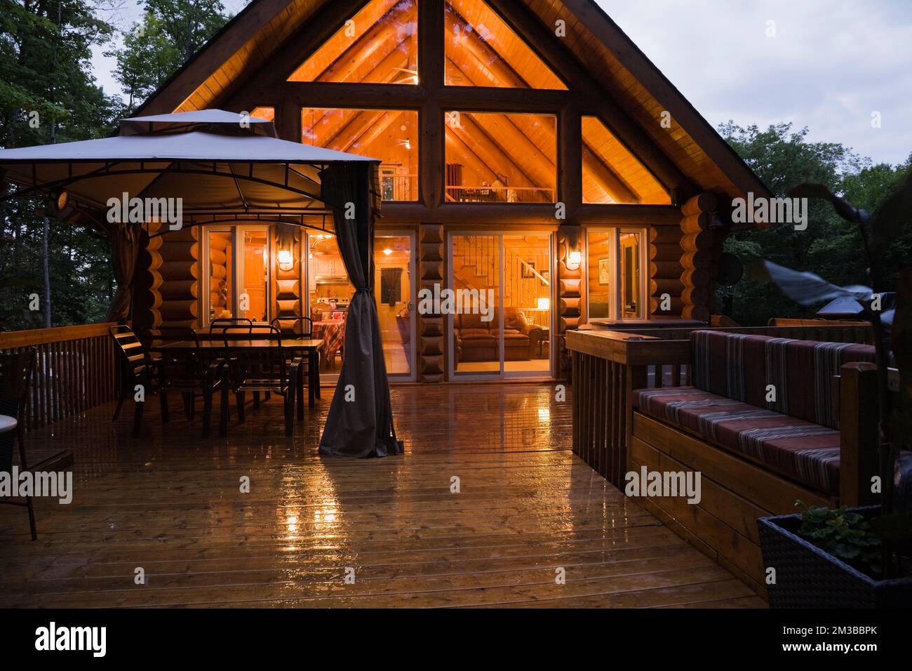 A-frame style log cabin with watered down wooden deck at dusk in summer ...