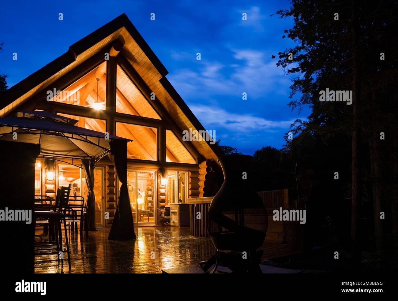 A-frame style log cabin with watered down wooden deck at dusk in summer ...