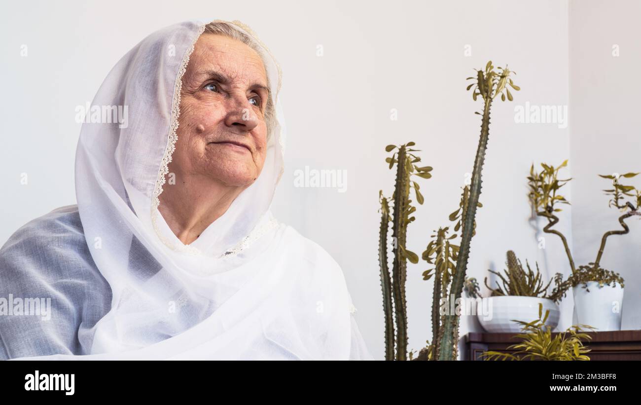 Portrait of old Muslim woman at eighties wearing white hijab sitting at ...