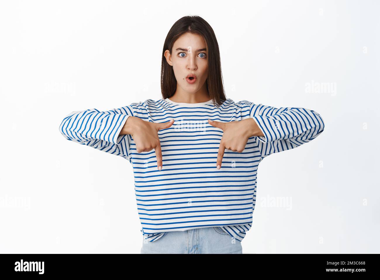 Portrait of intrigued young woman pointing fingers down, showing sale ...