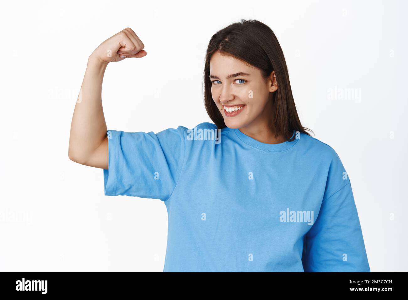 Portrait of smiling girl in t-shirt flexing biceps, showing arm muscle ...