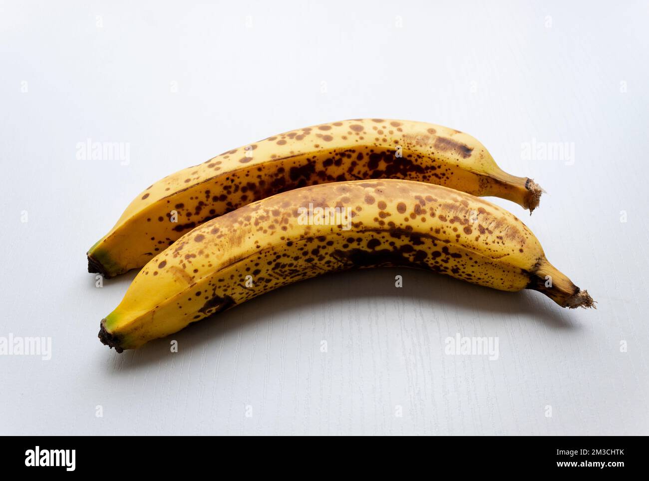 Close up to a two yellow freckled bananas in over a white wooden table ...