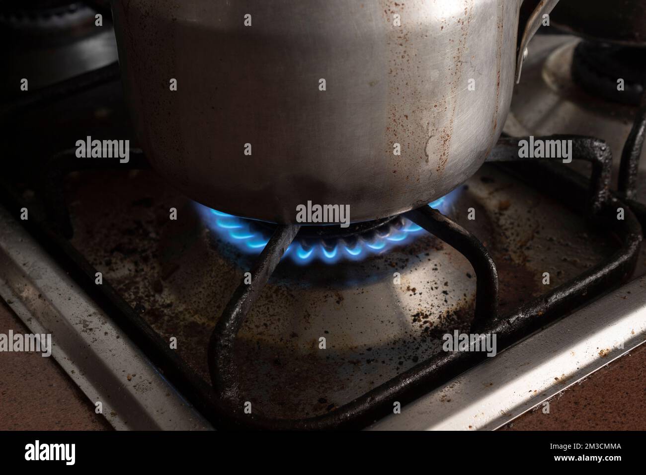 Closeup to a dirty natural gas stove on with dirty cocoa cooking pot ...
