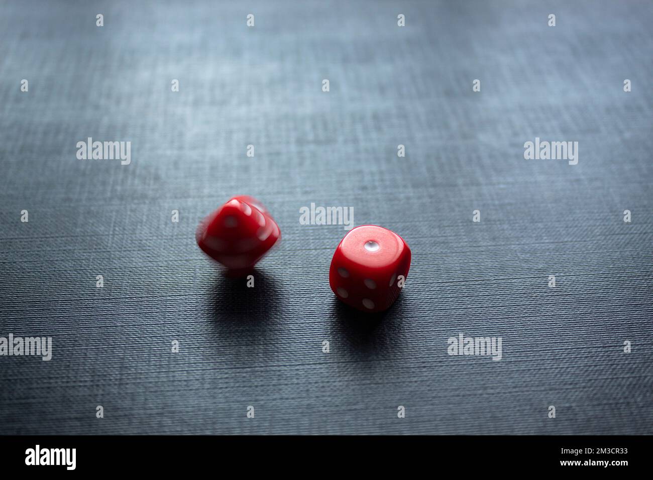 Closeup to a red dices, one dice is spinning over a black background ...