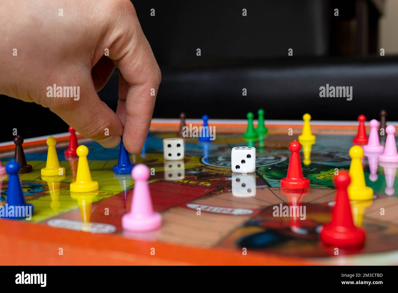 Male hand holding a blue pawn with old dices and color pawns over ...