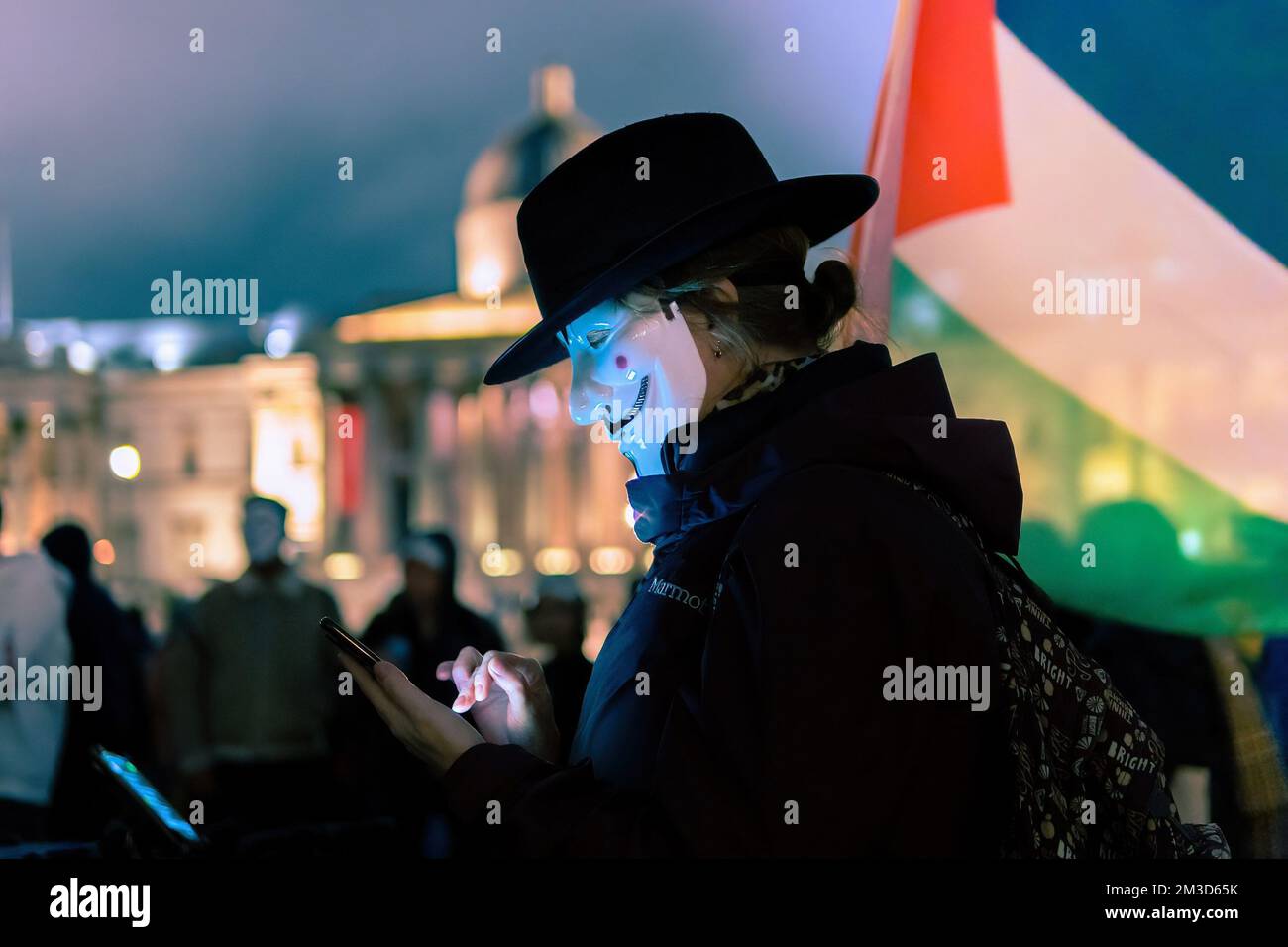 A protester wearing a Guy Fawkes mask holds a Palestinian flag during ...