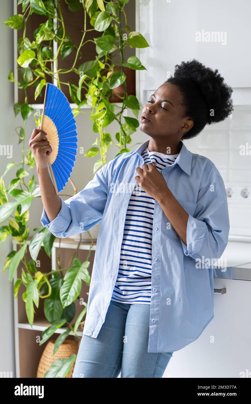 Young African American woman in blue shirt fanning herself with hand ...