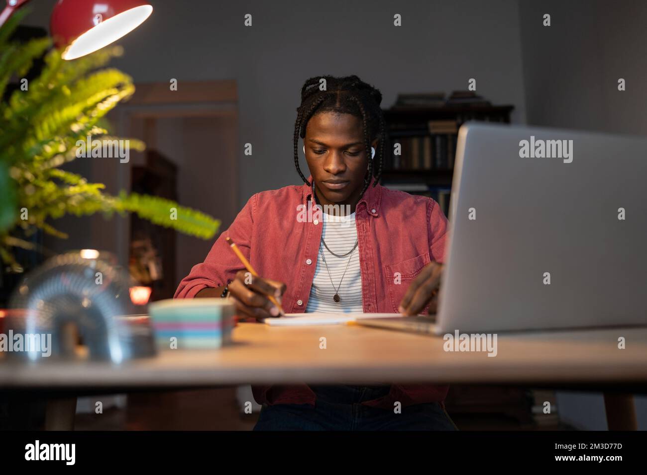 Hardworking young African guy student writing notes while watching ...