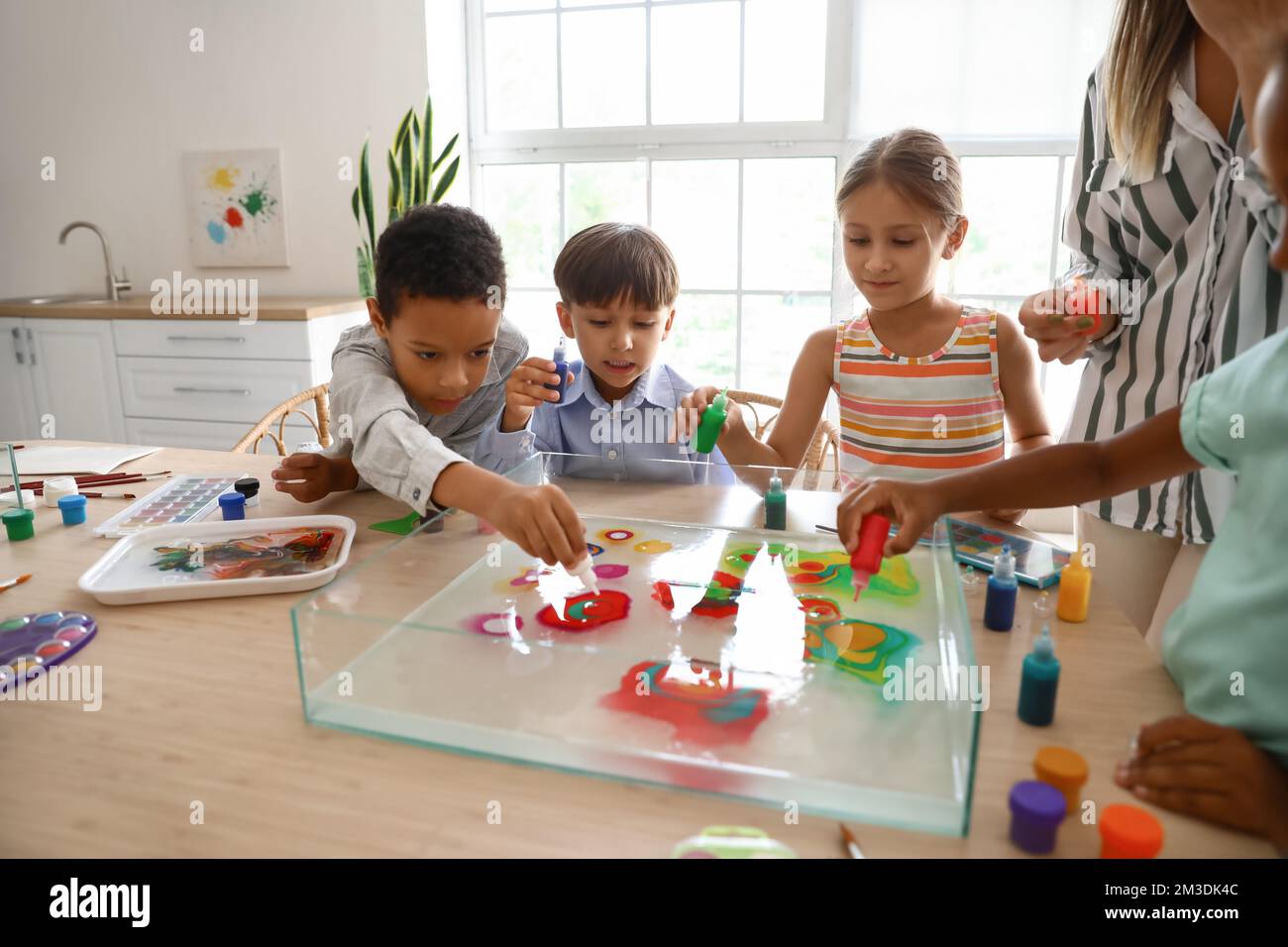 Little children with teacher pouring paints into water during master ...