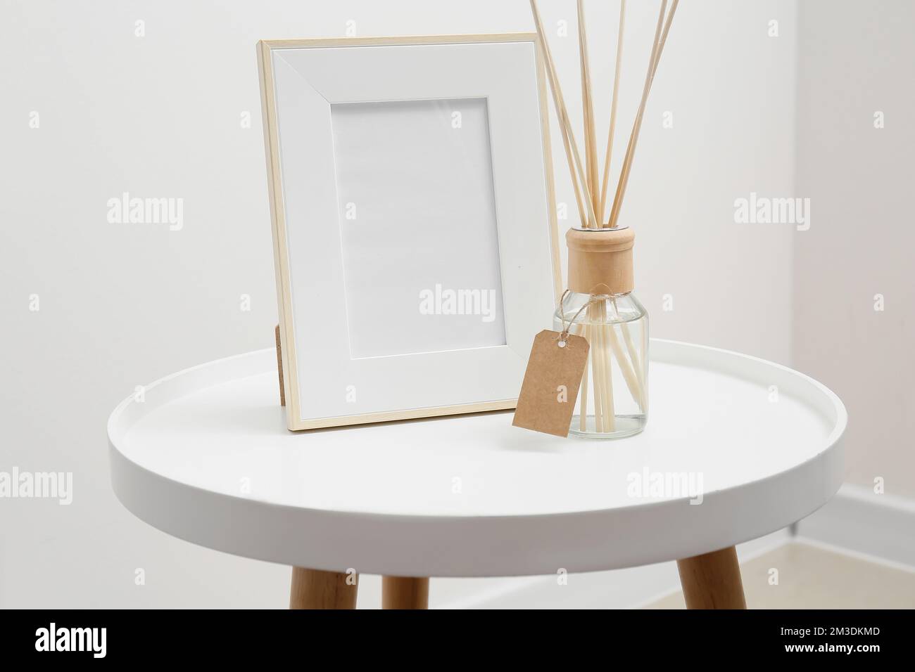 Blank photo frame and reed diffuser with card on table near white wall ...
