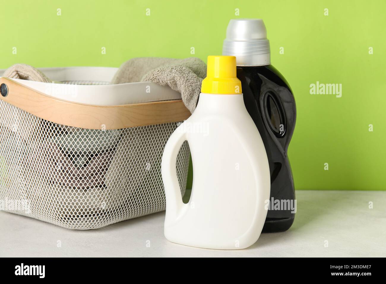 Laundry detergents and basket with clothes on table against green ...