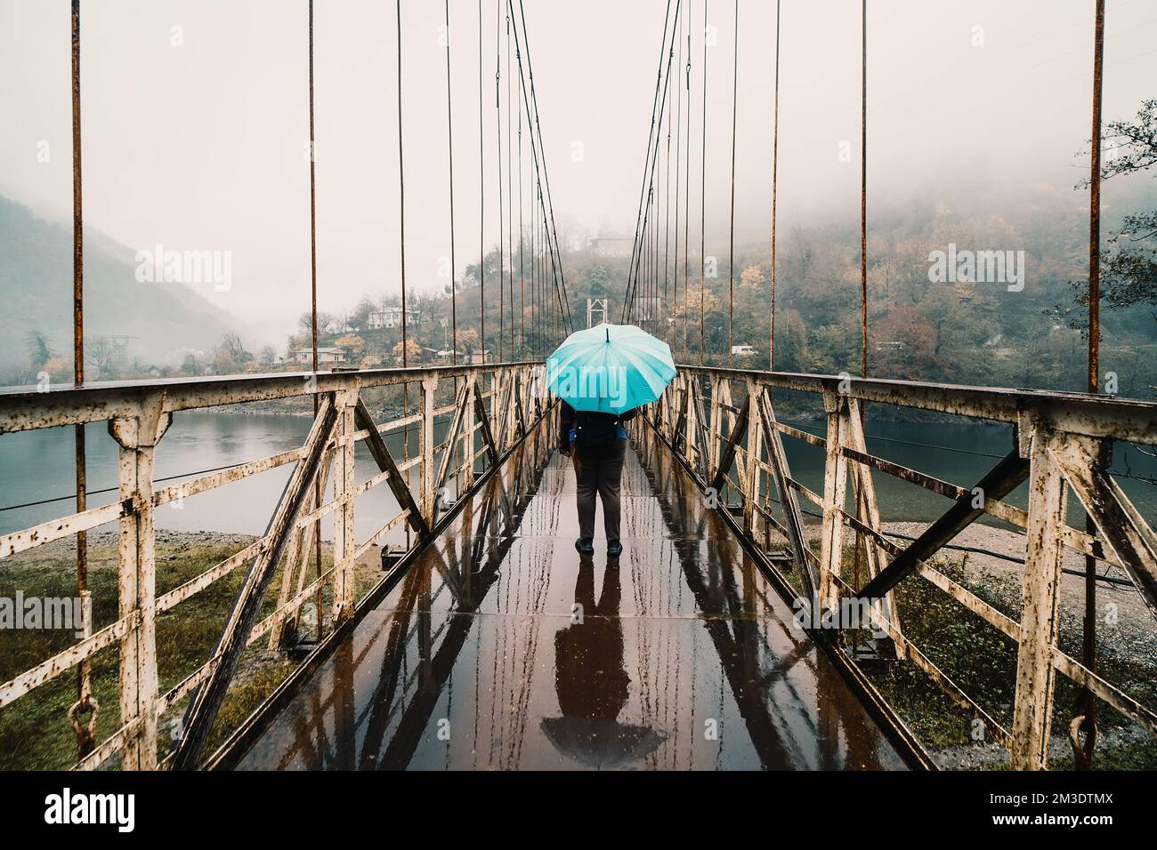 Girl with blue umbrella stands on wet iron suspension bridge in rainy ...