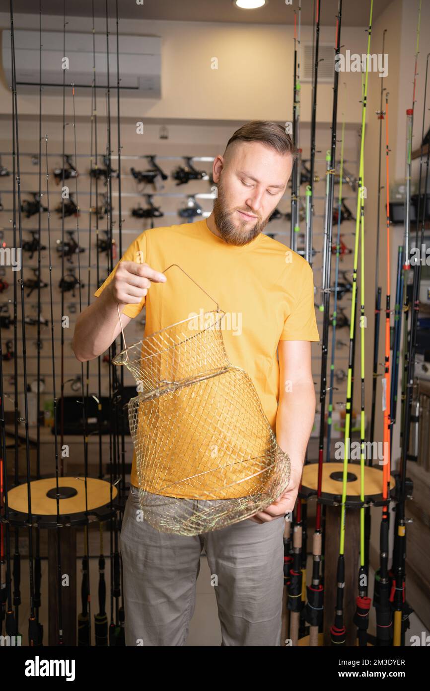 Young fisherman chooses a metal mesh for fish in a fishing store ...